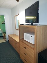 Quarto compacto com cômoda de madeira, micro-ondas e televisão por cima.