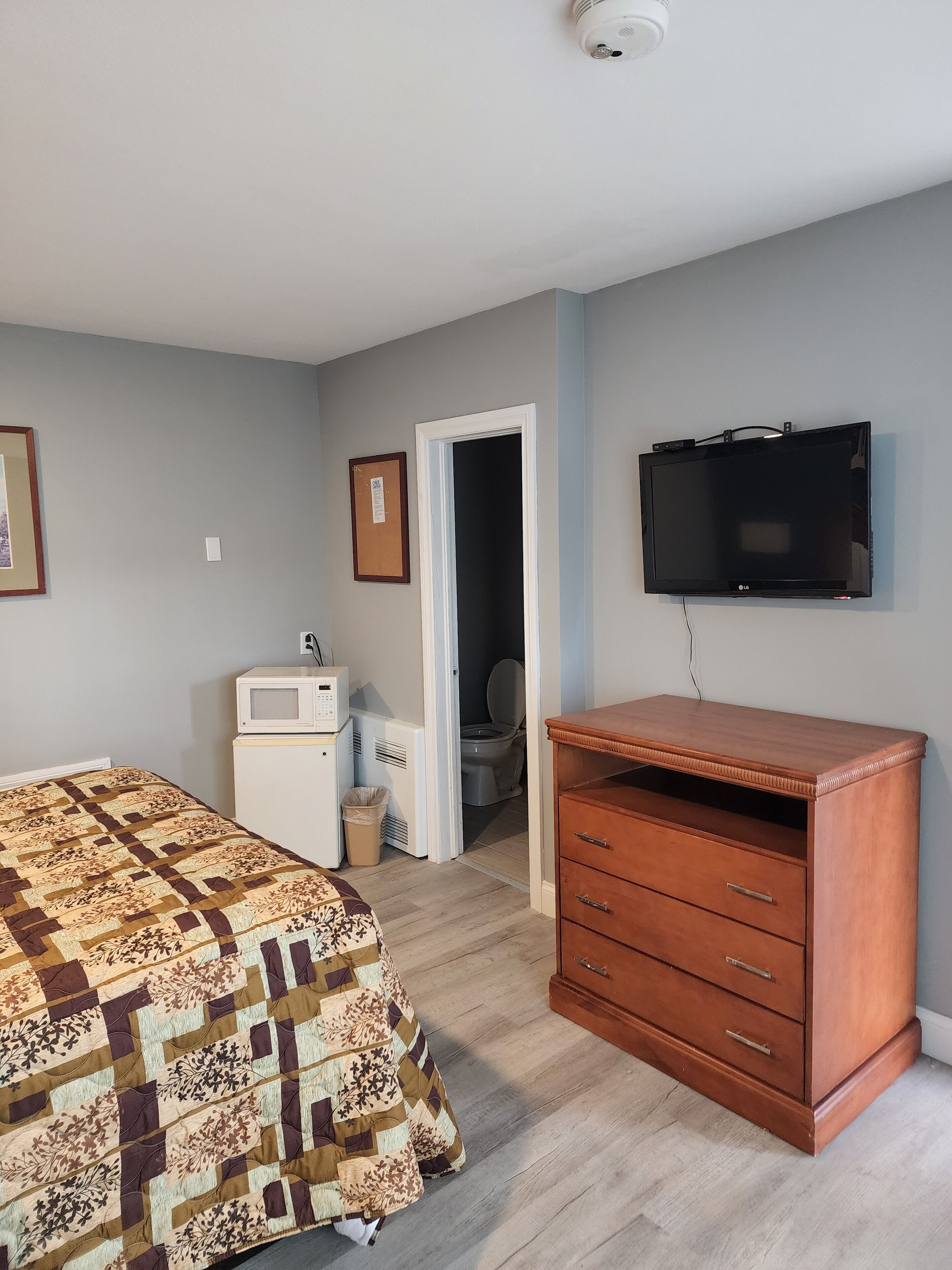 Quarto com cama, cómoda, televisão, micro-ondas e porta para uma casa de banho.