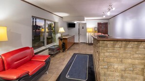 Um espaço de estar compacto com um sofá vermelho, uma parede de destaque em pedra, uma TV na parede e uma pequena cozinha com bancada e armários.