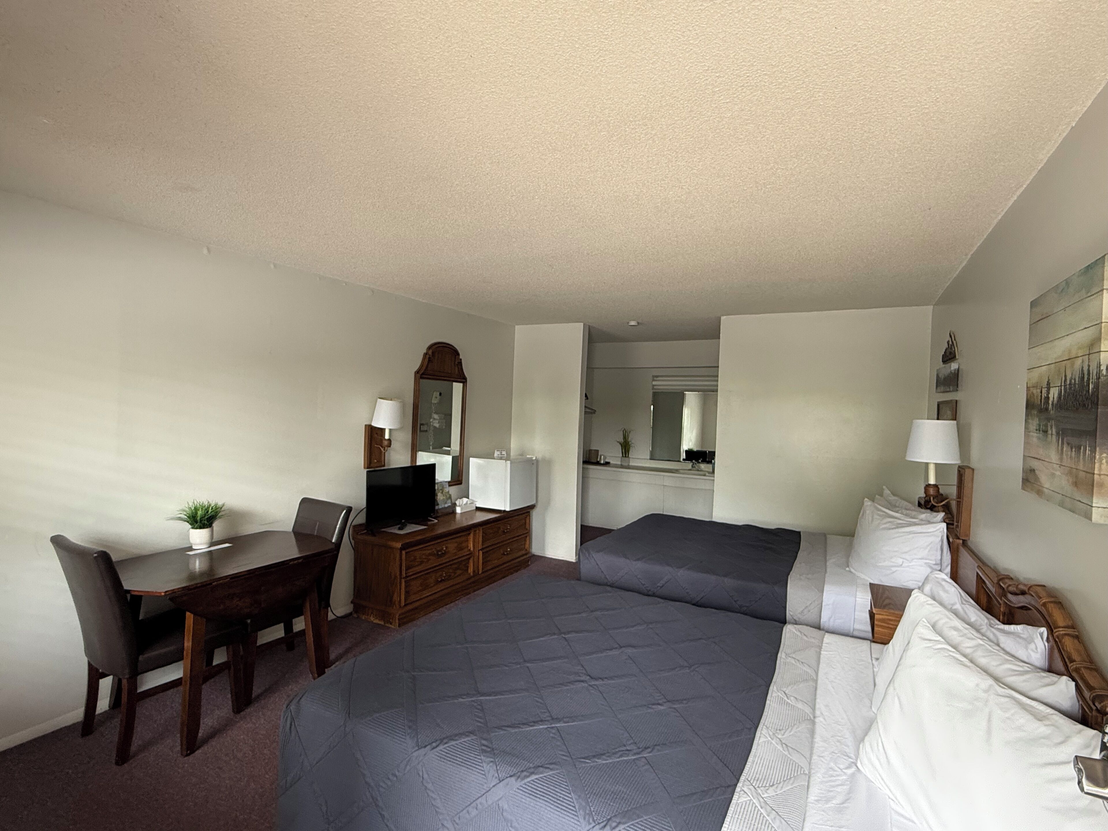 Quarto de hotel com cama, escrivaninha com computador, cadeira, cômoda e espelho.