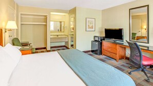 Quarto de hotel com cama, escrivaninha com computador, televisão, micro-ondas e armário.