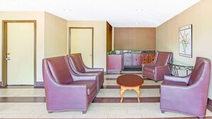 Um hall com poltronas de couro, uma pequena mesa de madeira e uma área de cozinha ao fundo.