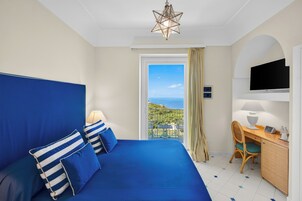 Quarto de hotel com cama, escrivaninha, cadeira, televisão e varanda com vista.