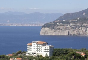 Um hotel com vários andares e telhado vermelho, situado perto de uma costa com falésias e vista para o mar.