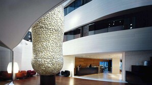 Um lobby moderno com uma escultura de pedra única, piso de madeira e um balcão de recepção.