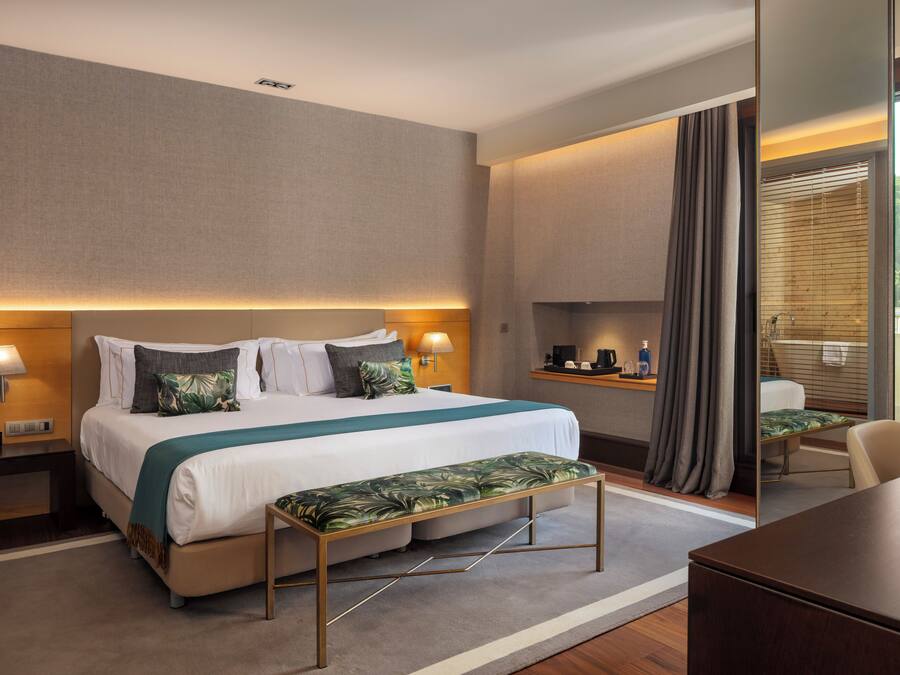 Quarto de hotel moderno com uma cama grande, luminárias de cabeceira, um banco e uma escrivaninha.