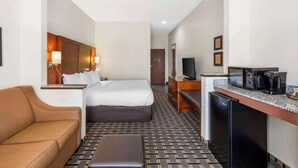 Quarto de hotel com cama, sofá, escrivaninha com cafeteira, televisão e geladeira.