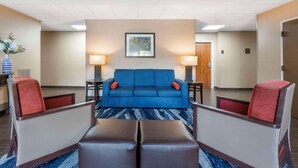 Um hall de hotel com um sofá azul, duas poltronas, uma mesa de centro e um quadro emoldurado na parede.