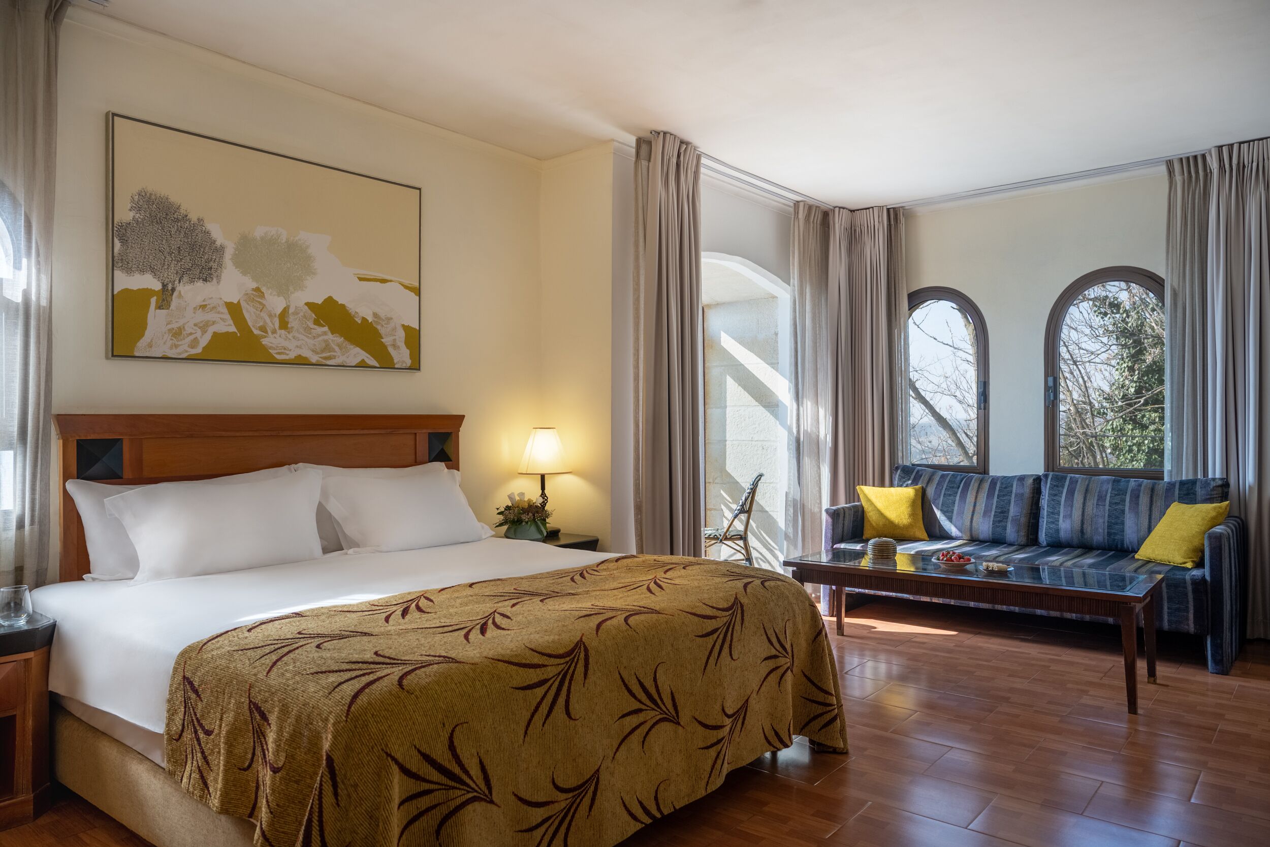 Quarto de hotel com uma cama grande, um sofá, uma mesa de centro e um quadro na parede.