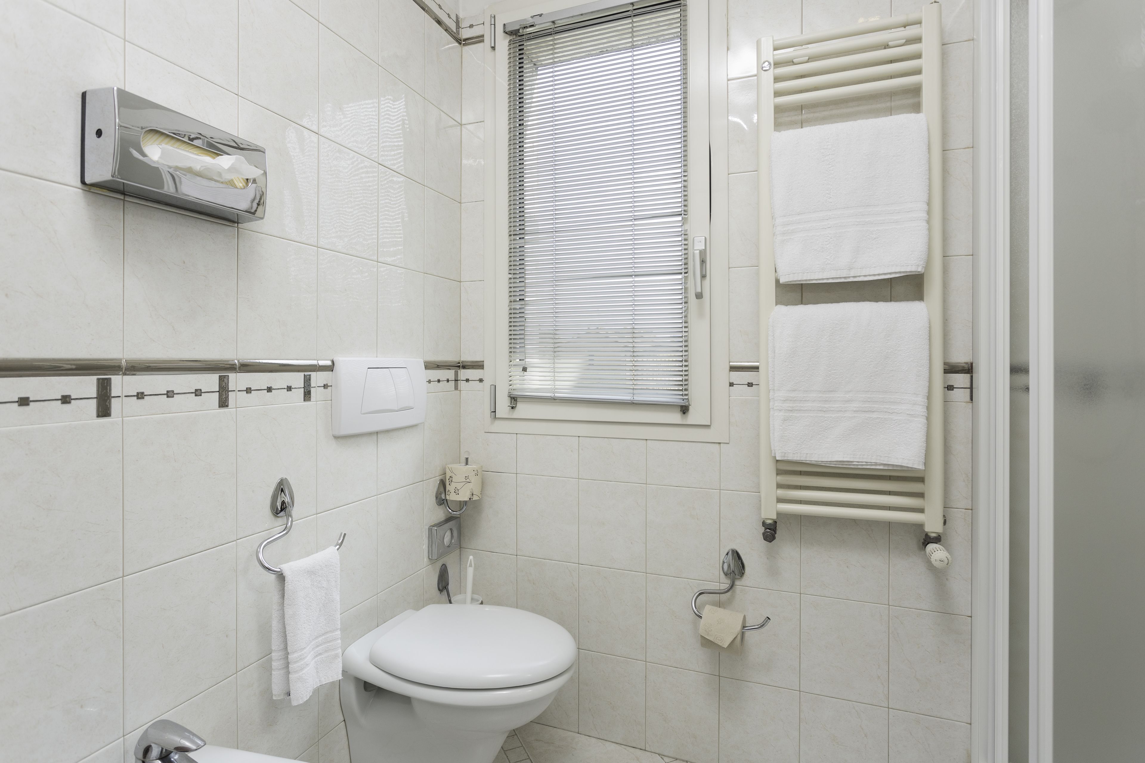 Casa de banho pequena e moderna com sanita, toalheiro, janela e aquecedor de toalhas.