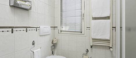 Casa de banho pequena e moderna com sanita, toalheiro, janela e aquecedor de toalhas.