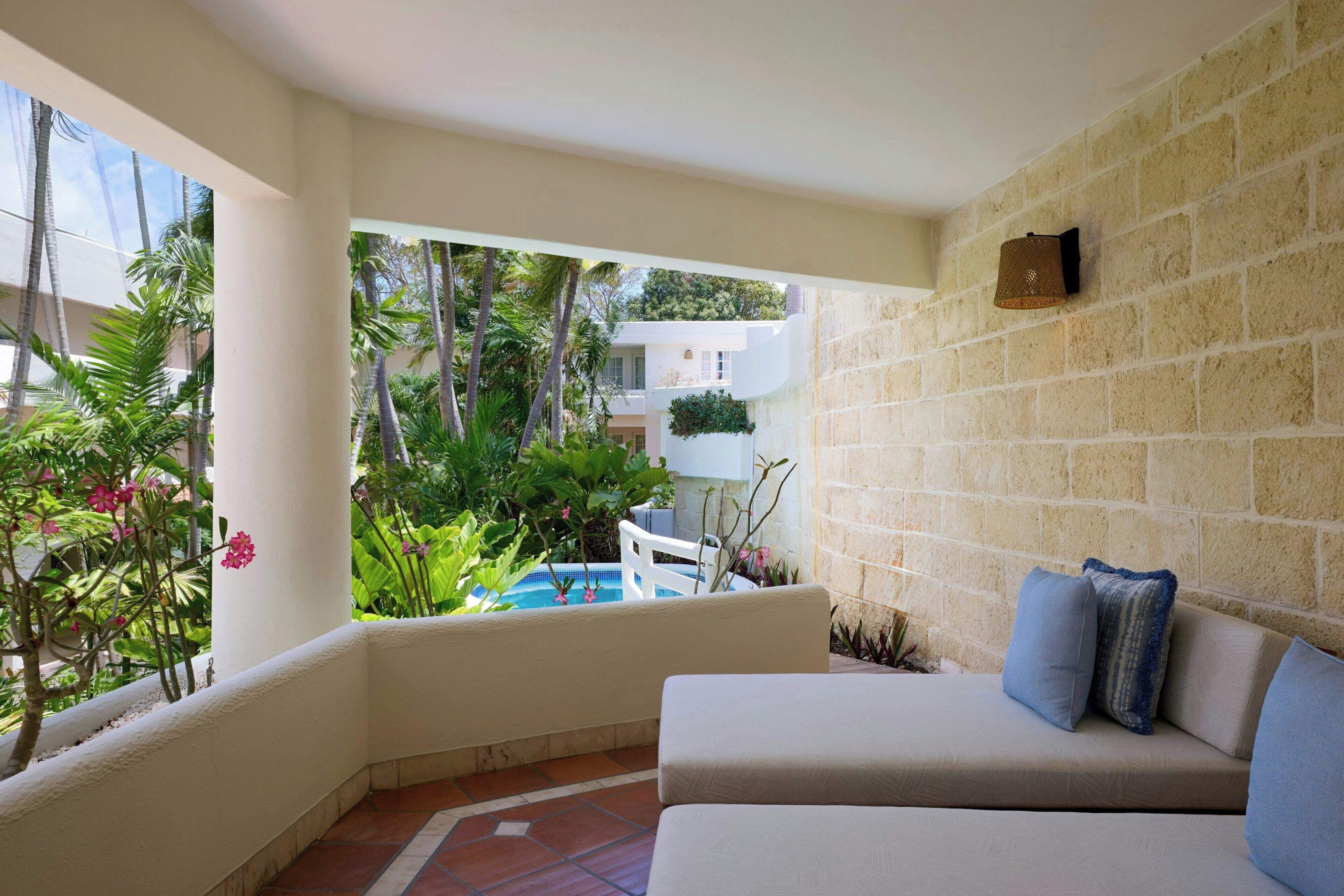 Interior moderno com um sofá branco, parede de pedra e vista para uma piscina e vegetação lá fora.