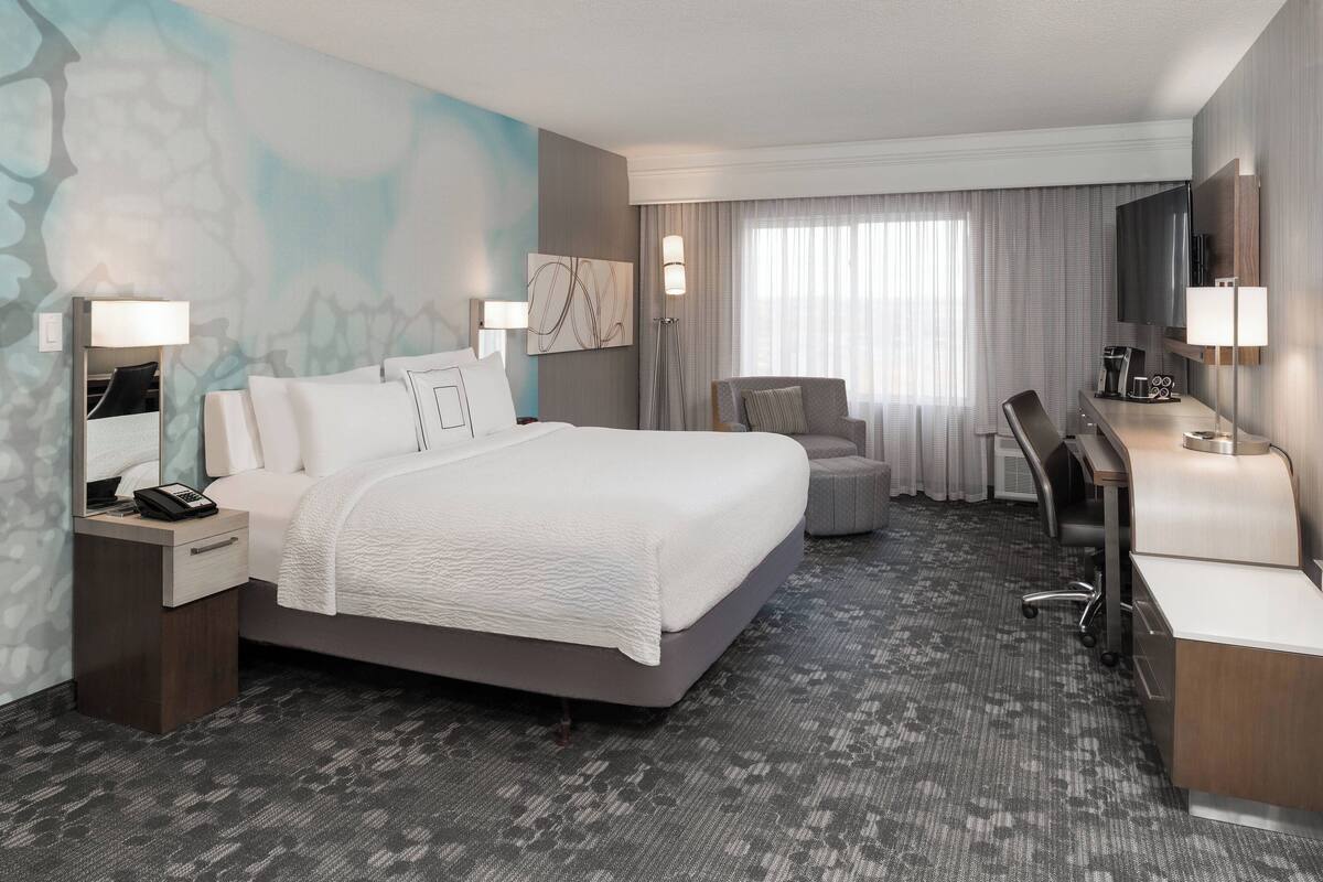 Quarto de hotel com uma cama grande, uma escrivaninha, uma cadeira e uma televisão.