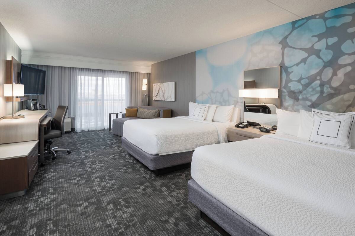 Quarto de hotel com duas camas, uma escrivaninha, uma cadeira, uma televisão e um quadro abstrato grande na parede.
