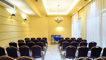 Sala de conferência com fileiras de cadeiras voltadas para uma mesa com toalha azul, um candelabro e luminárias fixadas na parede.
