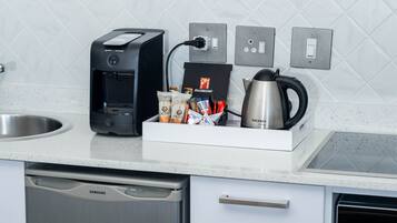 Uma cozinha com cafeteira, chaleira e suporte para cápsulas de café no balcão.