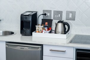 Uma cozinha com cafeteira, chaleira e suporte para cápsulas de café no balcão.