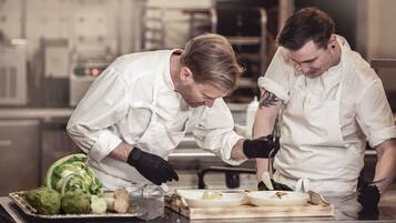 Dois chefs preparando alimentos em uma cozinha profissional com superfícies de aço inoxidável e equipamentos modernos.