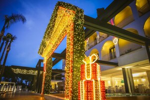 Um edifício com uma grande estrutura iluminada com o número '1' e caixas de presente, cercado por palmeiras e uma área de piscina.