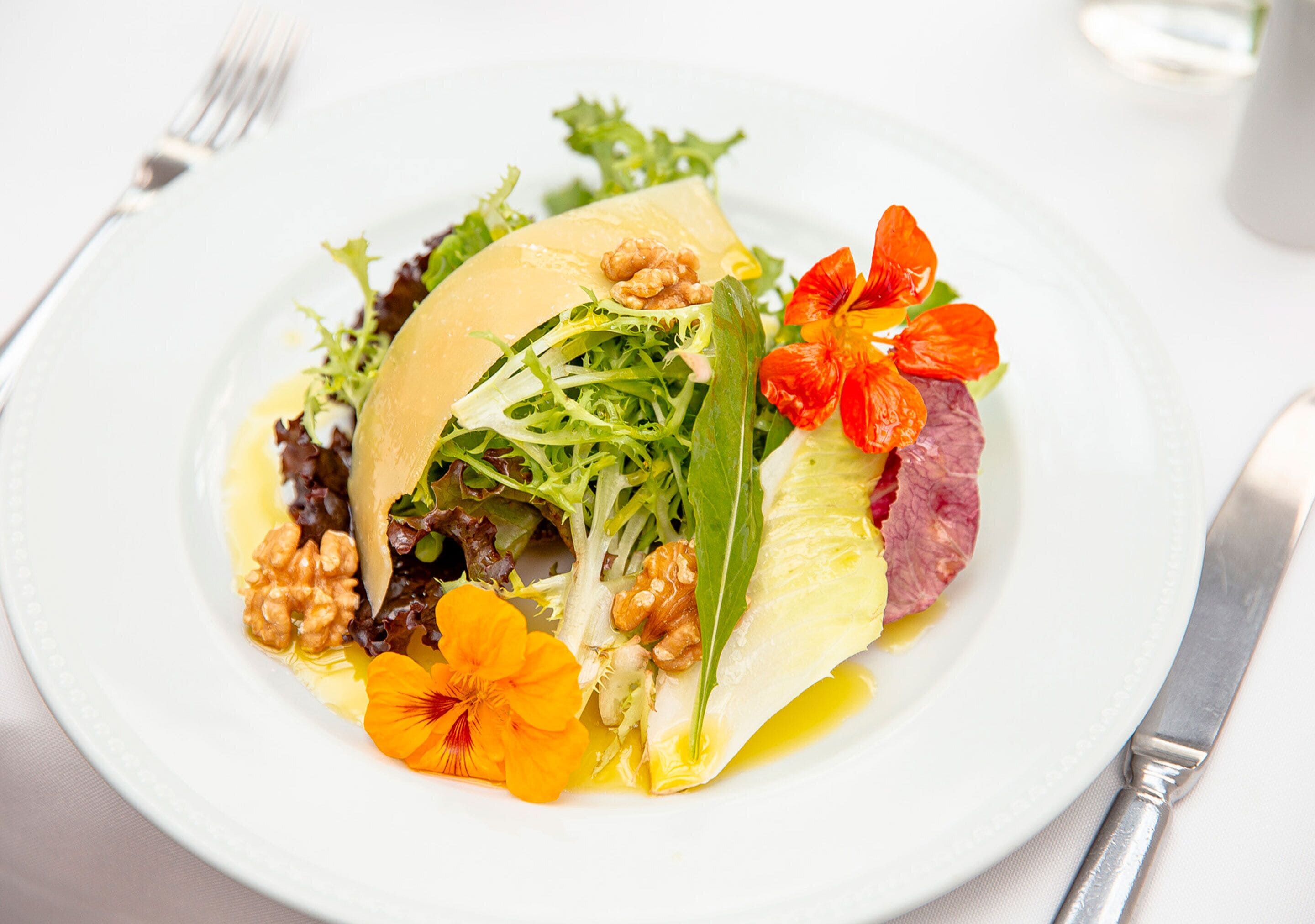Um prato branco com salada, nozes e flores.