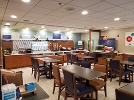 Um café moderno com mesas e cadeiras de madeira, um balcão de pastelaria e um espaço para refeições da manhã.
