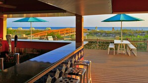 Um deck de madeira com área de bar, assentos ao ar livre e guarda-sóis com vista para a praia.