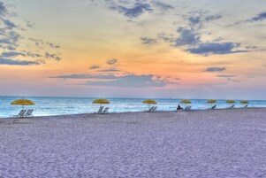Uma praia com fileiras de espreguiçadeiras e guarda-sóis.