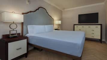 Quarto de hotel com cama, mesas de cabeceira com luminárias, televisão e cômoda.