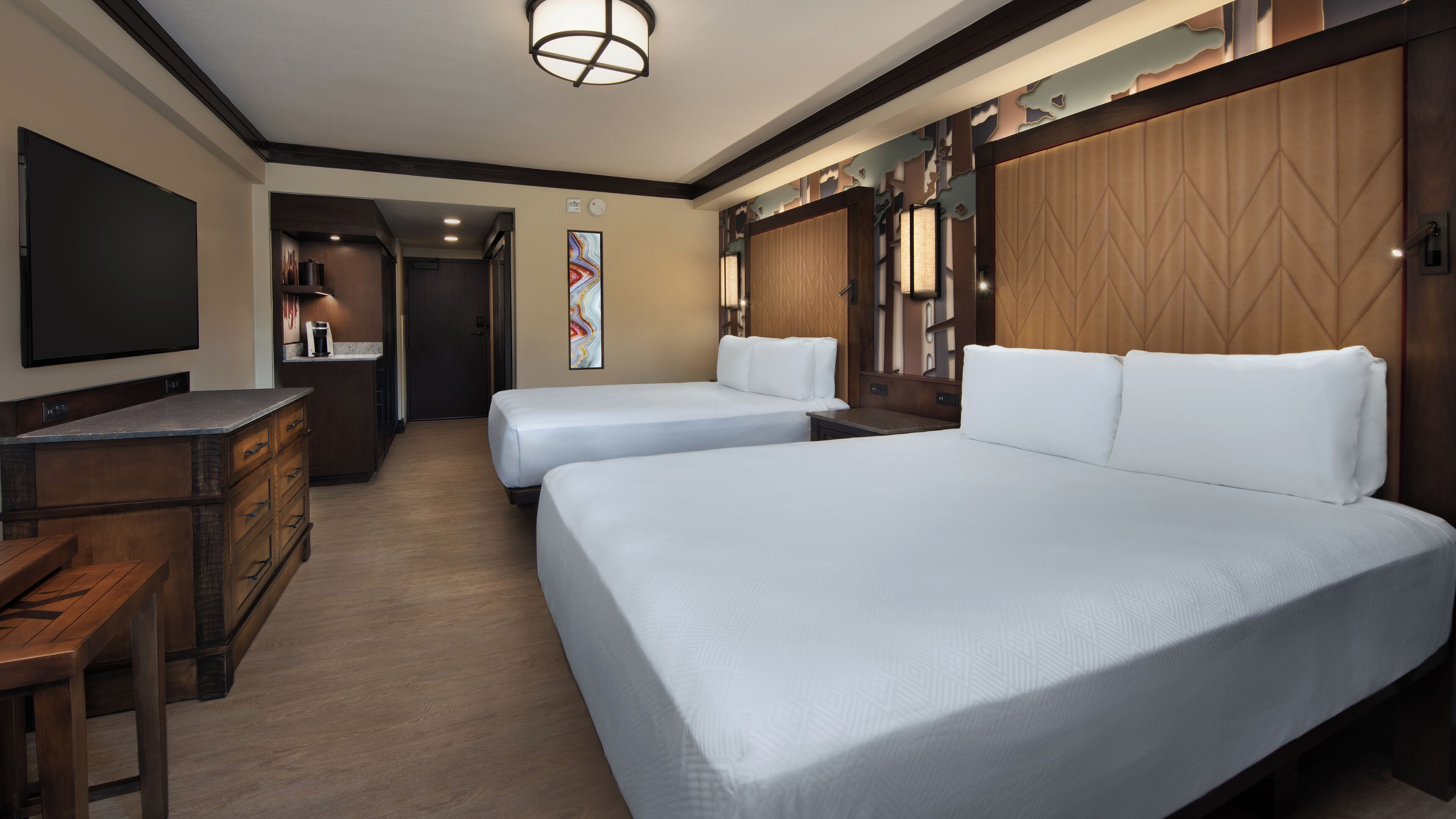 Quarto de hotel com duas camas, uma escrivaninha, uma cadeira e uma televisão.