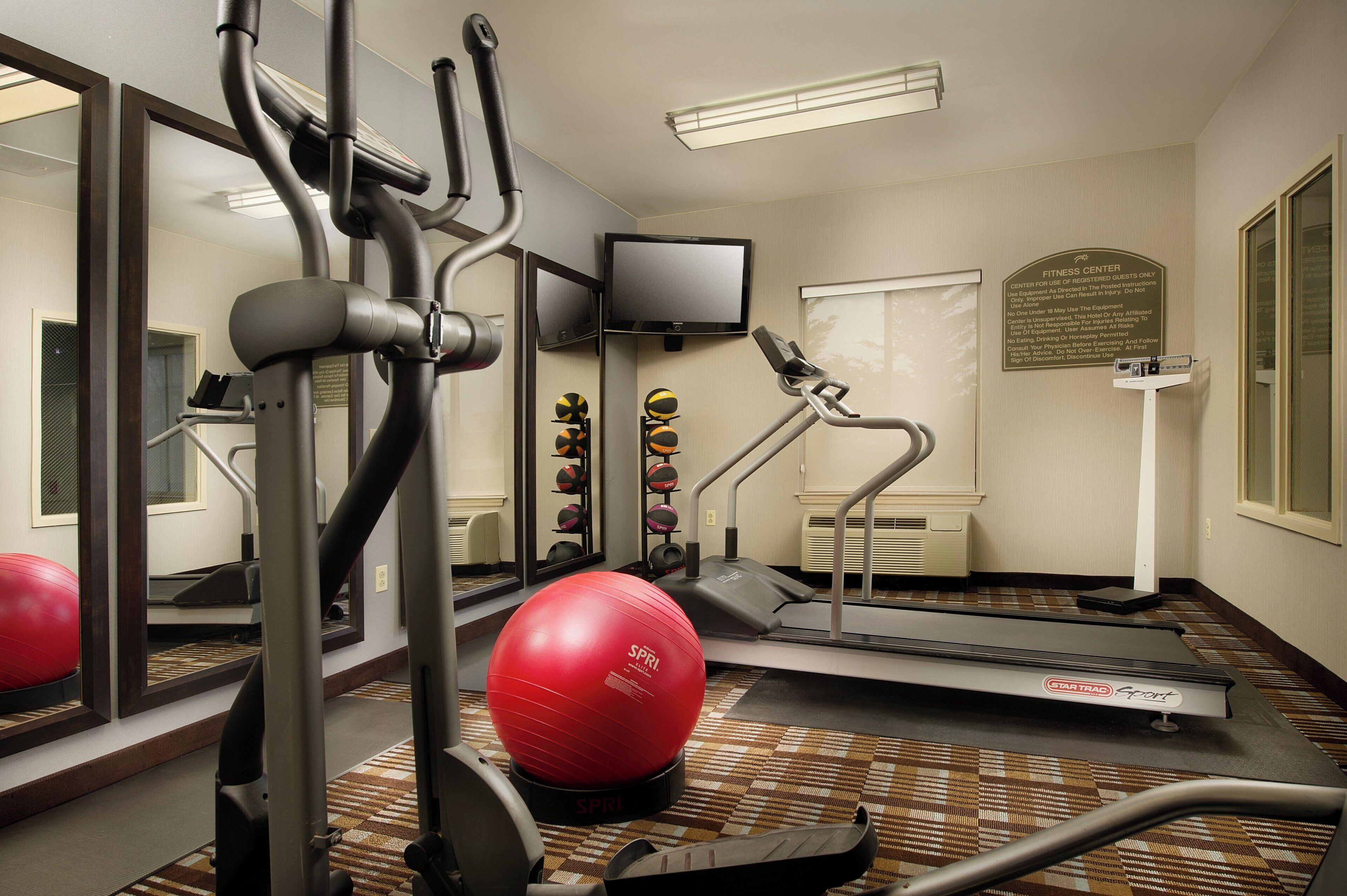 Centro de ginástica com equipamentos de exercício, esteira e espelho.
