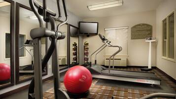 Centro de ginástica com equipamentos de exercício, esteira e espelho.