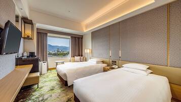 Quarto de hotel com duas camas, uma escrivaninha, televisão e vista para as montanhas.
