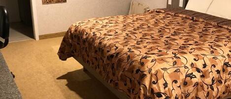 Quarto de hotel com uma cama, uma secretária pequena, uma cadeira, uma porta e um quadro na parede.