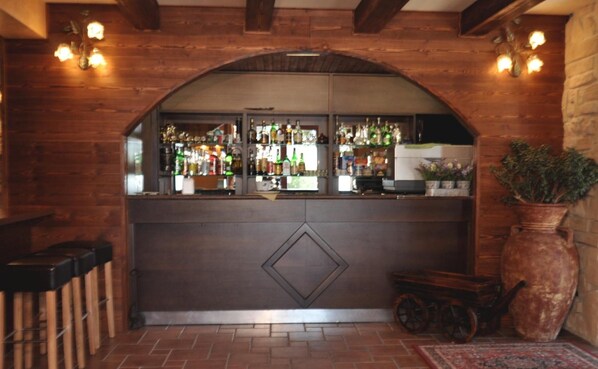 Uma área de bar com arco de madeira, prateleiras com garrafas, padrão de diamante decorativo no balcão e uma grande planta em vaso.
