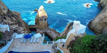 Um hotel à beira-mar com piscina, uma escadaria que leva até a falésia e vista para o mar.