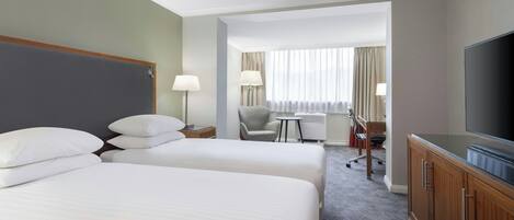 Quarto de hotel com duas camas, uma escrivaninha, uma cadeira, uma televisão e uma janela com cortinas.