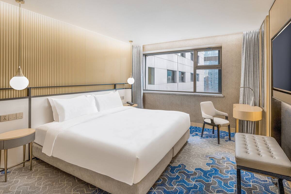 Quarto de hotel com uma cama grande, uma escrivaninha, uma cadeira e uma televisão.