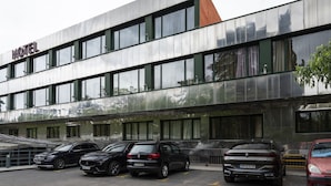 Um hotel moderno com fachada espelhada, várias janelas e um estacionamento com diversos carros.