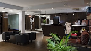 Um hall de hotel moderno com balcão de recepção, área de estar e uma grande planta em vaso.