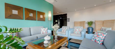 Um hall de hotel moderno com uma parede azul-esverdeada, uma mesa de centro de madeira e dois sofás com almofadas estampadas.