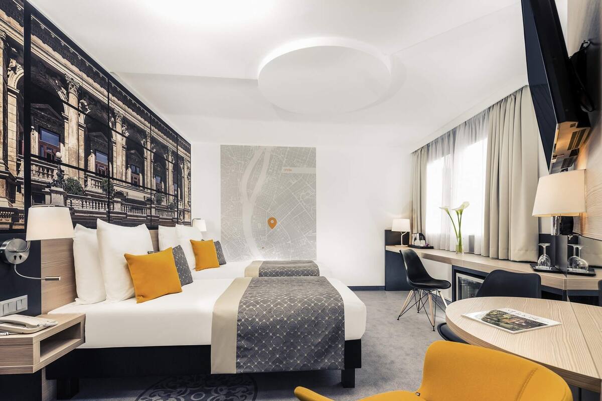 Quarto de hotel com uma cama grande, uma escrivaninha, uma cadeira e um mapa na parede.