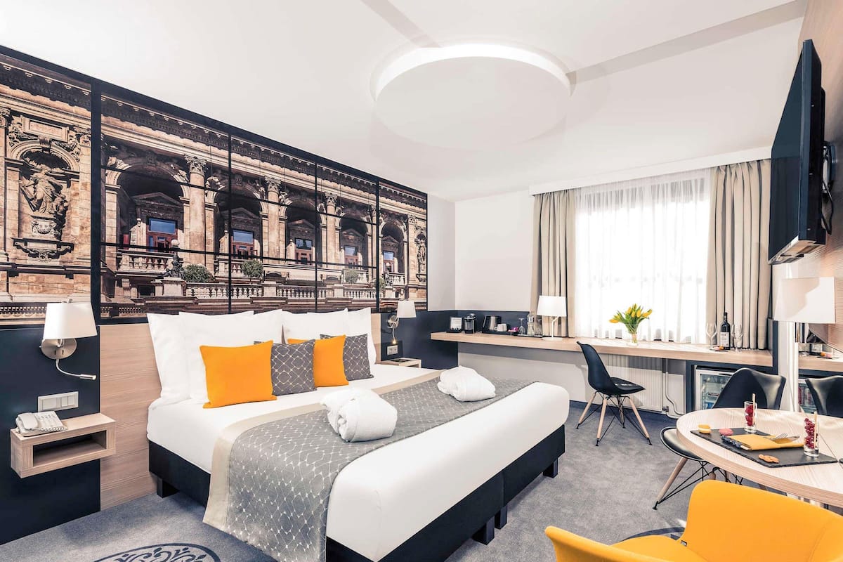 Quarto de hotel com uma cama grande, uma escrivaninha, uma cadeira e uma televisão.