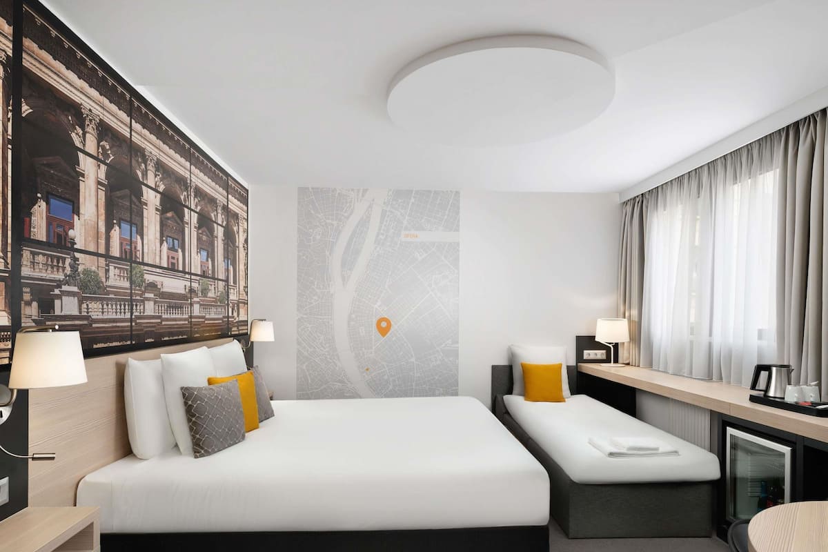 Quarto de hotel com uma cama grande, uma escrivaninha, uma cadeira e um mapa na parede.