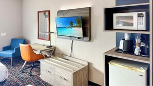 Quarto de hotel com televisão na parede, micro-ondas, pequeno frigorífico, secretária com cadeira e uma cama.