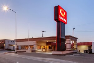 Um motel com um letreiro vermelho grande, um estacionamento e um poste de luz.