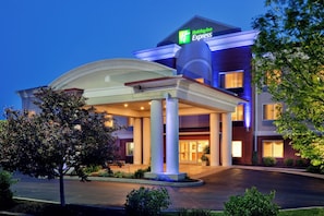 Um hotel Holiday Inn Express com entrada coberta, colunas e área ajardinada com árvores.