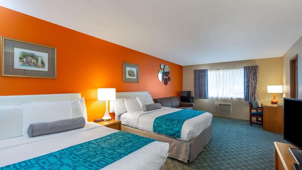 Quarto de hotel com duas camas, uma escrivaninha, televisão e janela com cortinas.
