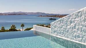 Uma piscina infinita azul e límpida com vista para o mar e montanhas ao fundo.