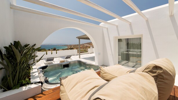 Terraço no telhado com hidromassagem, almofadas bege e vista para o mar.