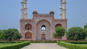 Um edifício grande e simétrico com duas minaretes altas e um arco central, cercado por vegetação bem cuidada.